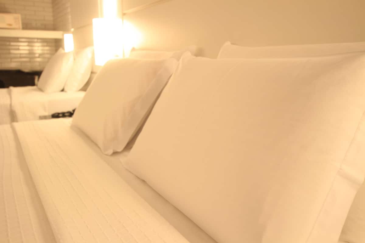 Quarto de hotel com cama, almofadas e mesa de cabeceira com abajur.