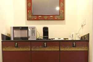 Uma cozinha compacta com micro-ondas, máquina de café e jarra de café em uma bancada.