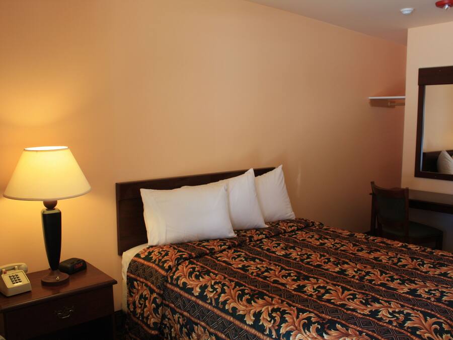 Quarto de hotel com cama, mesa de cabeceira com luminária e telefone, e um espelho na parede.