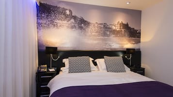 Quarto de hotel com uma cama grande, duas mesas de cabeceira, um criado-mudo, telefone fixado na parede e um grande mural paisagístico.