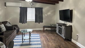 Uma sala de estar com um sofá de couro marrom, uma mesa de centro de vidro, uma televisão e uma lareira.