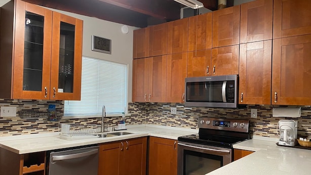 Uma cozinha moderna com armários de madeira, lava-louças de aço inoxidável, micro-ondas, forno e painel de azulejos.
