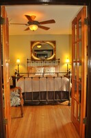 Quarto com cama, piso de madeira, ventoinha no teto e duas luminárias de cabeceira.