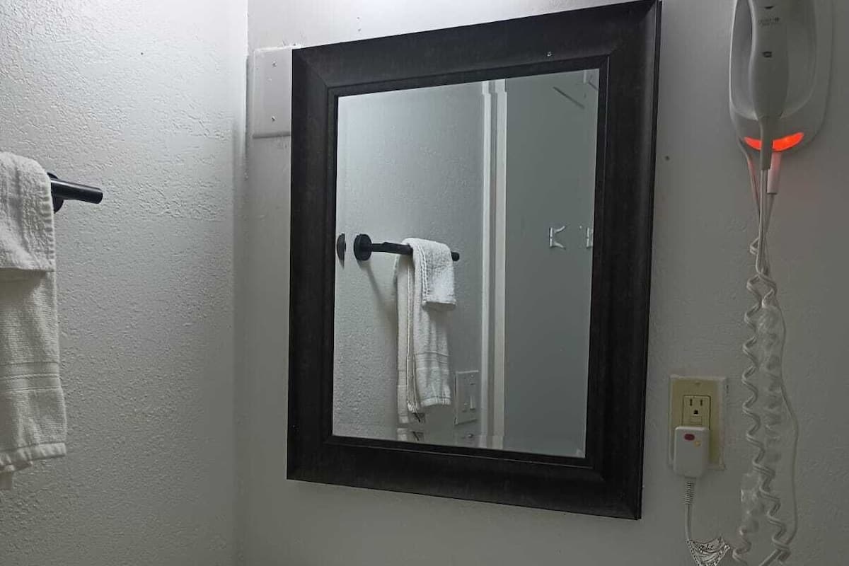 Casa de banho com uma sanita branca, espelho e secador de cabelo fixado na parede.