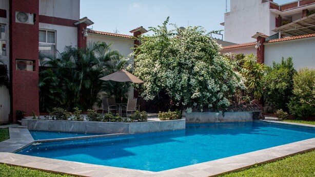 Piscina cercada por um jardim bem cuidado, com diversas plantas e um espaço de estar com cadeiras.