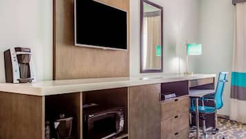 Quarto de hotel com televisão de tela plana, cafeteira, micro-ondas, escrivaninha com cadeira e abajur.
