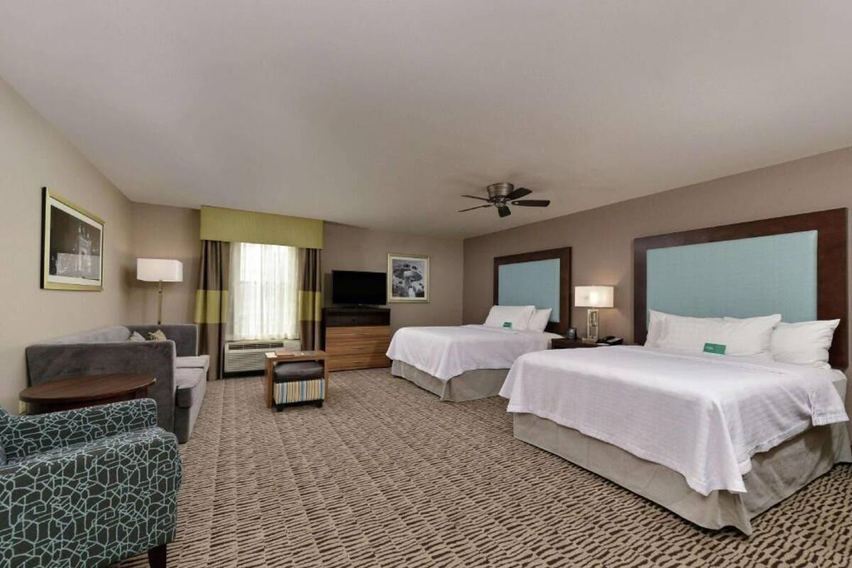 Quarto de hotel com duas camas, um sofá, uma TV e um ventilador de teto.