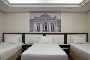 Quarto de hotel com duas camas de solteiro, mesa de cabeceira, TV de tela plana e uma grande moldura com uma imagem de um edifício na parede.