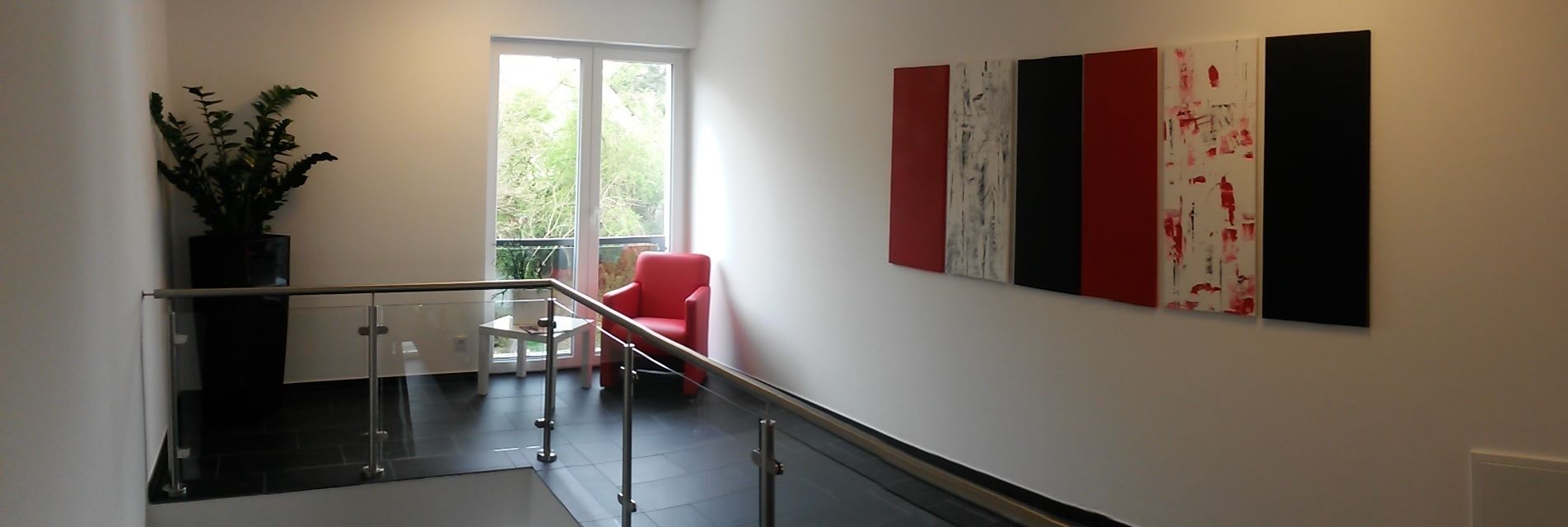 Um interior moderno com escadaria, uma cadeira vermelha e arte abstrata na parede.