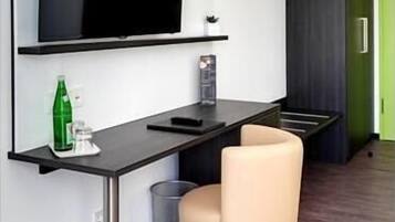 Uma cozinha moderna com bancada preta, uma TV instalada acima dela, uma garrafa verde e uma lixeira.