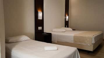 Quarto de hotel com duas camas de solteiro, uma mesa de cabeceira e iluminação na parede.