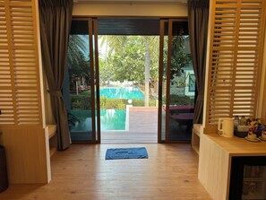 Quarto com vista para uma piscina, piso de madeira e um banco.