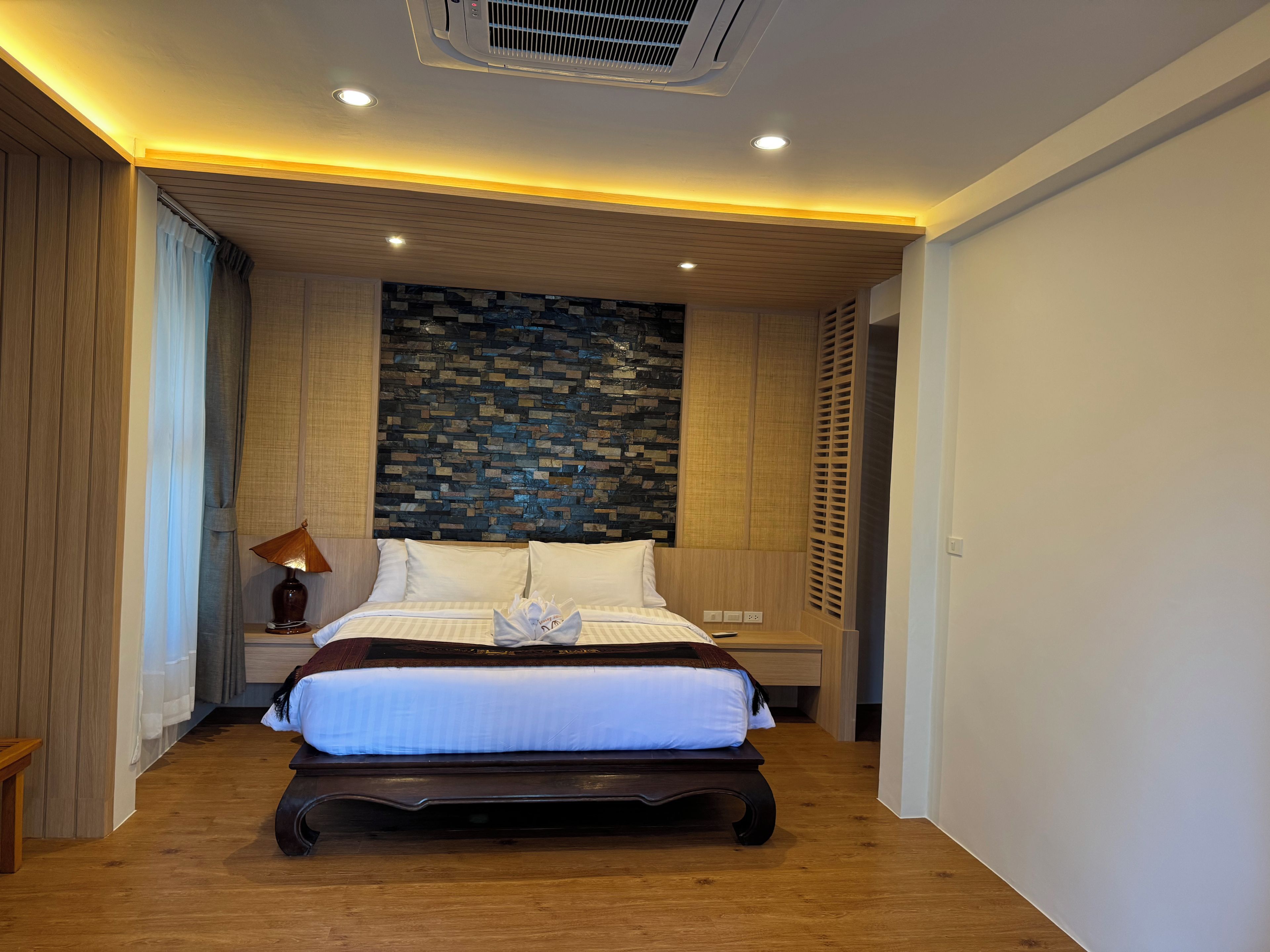 Cama bem arrumada com cabeceira, luminária lateral e parede com textura.