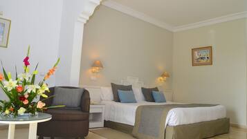 Quarto de hotel com uma cama, uma cadeira, uma mesinha com flores e um quadro na parede.