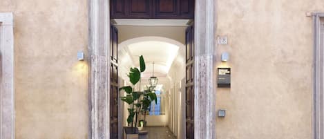 Entrada de hotel com um arco central, uma planta em vaso e uma placa indicando a localização.
