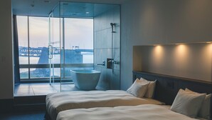 Quarto de hotel moderno com uma cama grande, uma banheira e box de vidro.