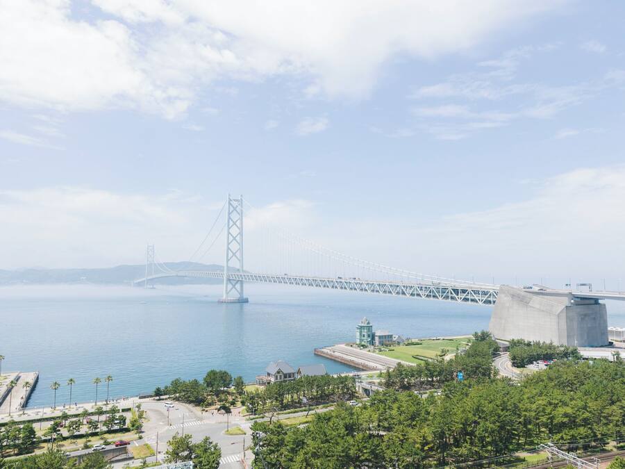 Paisagem costeira urbana com uma ponte imponente, um farol e uma grande estrutura de concreto.