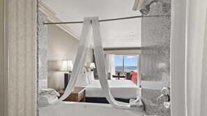 Quarto de hotel moderno com uma banheira grande, duas camas, vista para o mar e uma varanda.