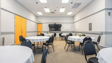 Uma sala de conferências com várias mesas e cadeiras, uma tela grande e um quadro branco.