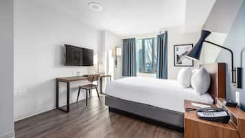 Quarto de hotel moderno com uma cama grande, uma escrivaninha com cadeira, televisão de tela plana, luminária de mesa, telefone e janela com cortinas.