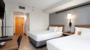 Quarto de hotel com duas camas, uma escrivaninha e uma mesa de cabeceira com abajur.