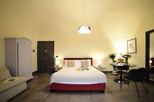 Quarto de hotel com cama, mesas de cabeceira, escrivaninha, cadeira, guarda-roupa e porta.
