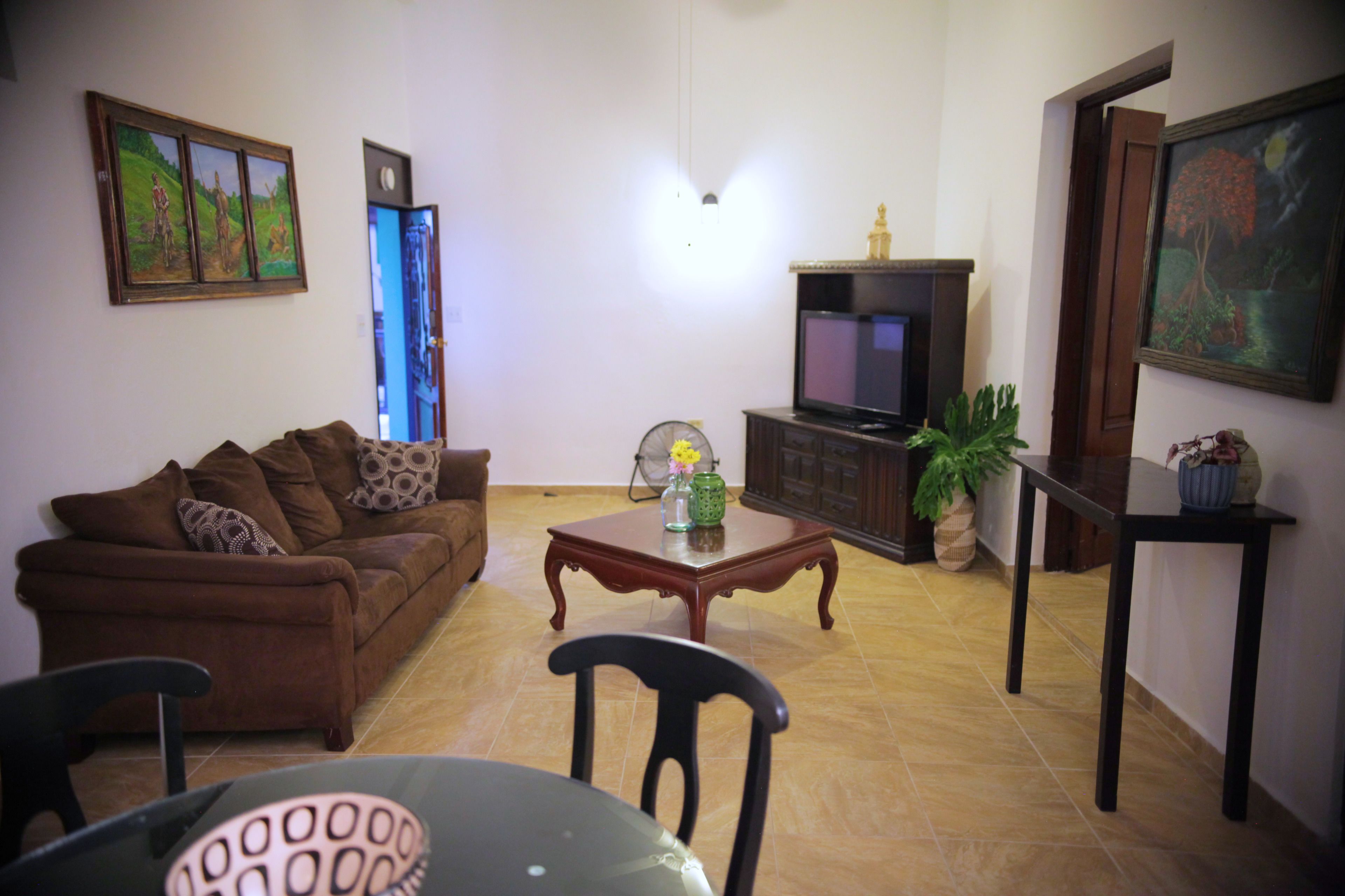 Uma sala de estar com um sofá marrom, uma mesa de centro de madeira, um rack para TV e um quadro na parede.