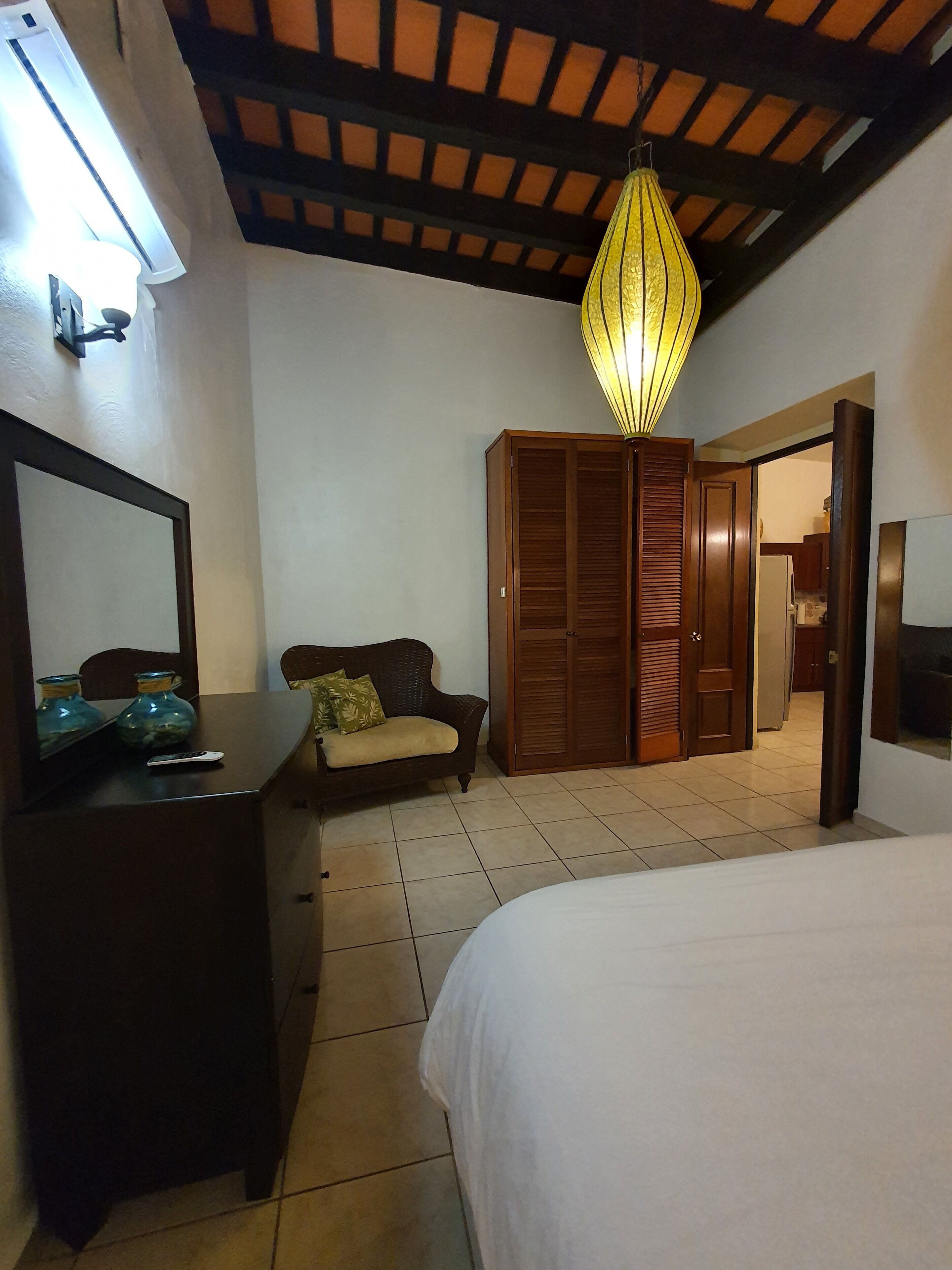 Quarto com cama, cômoda, guarda-roupa, sofá, luminária pendente e espelho.