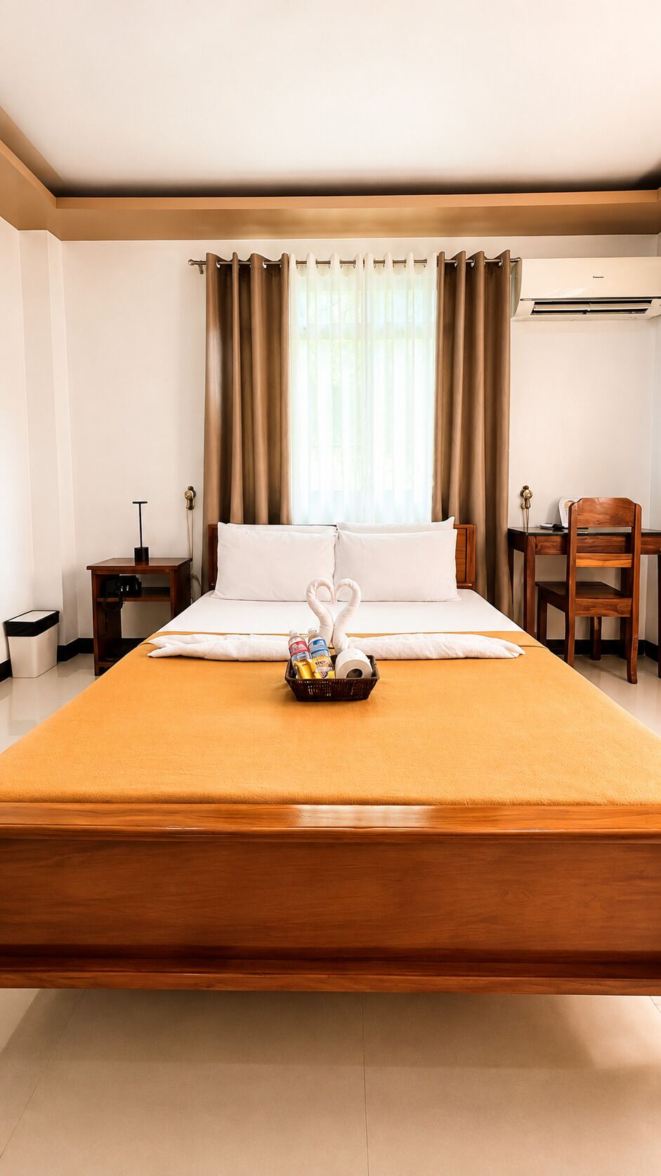 Quarto de hotel com uma cama grande, uma mesa, uma cadeira e uma janela com cortinas.