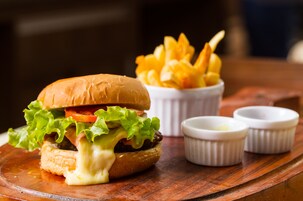 Um hambúrguer com batatas fritas e acompanhamentos sobre uma tábua de madeira.