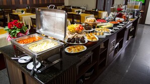 Buffet com diversos pratos e uma televisão ao fundo.