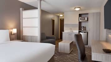 Quarto de hotel com uma cama grande, uma escrivaninha com cadeira, micro-ondas e um armário pequeno.