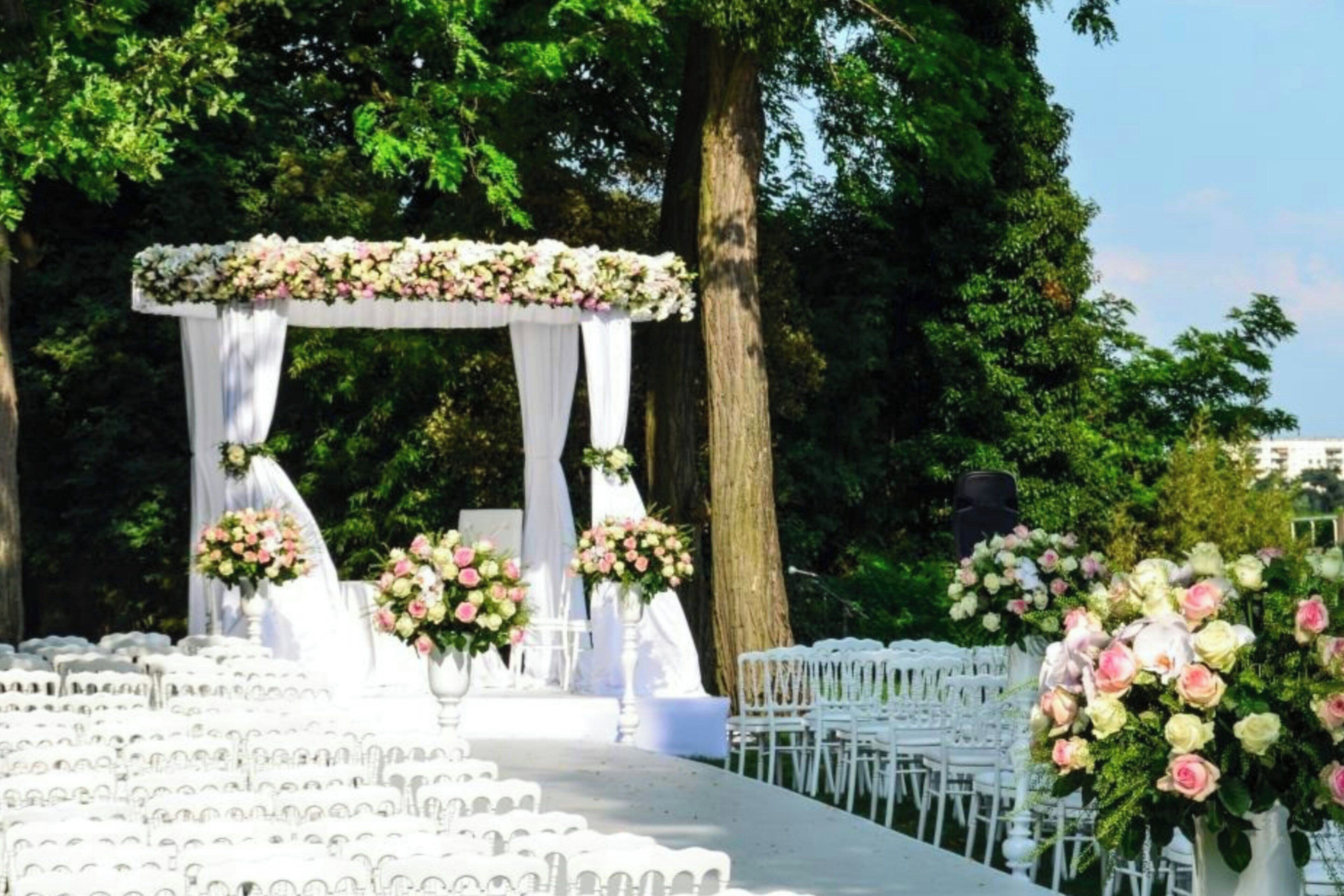 Decoração de casamento ao ar livre com um corredor branco, flores e cadeiras brancas.