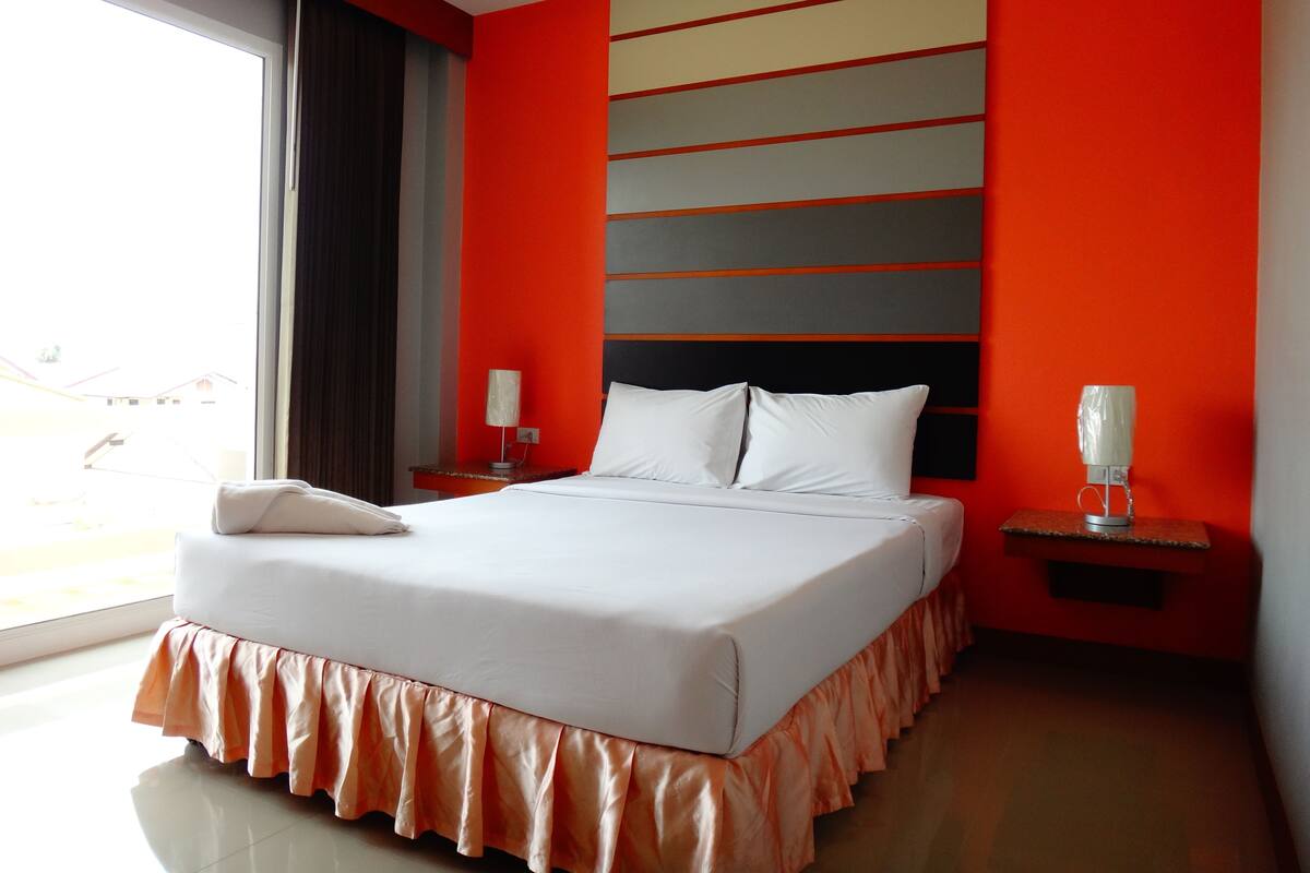 Quarto de hotel com uma cama grande, mesa de cabeceira, luminária e vista para o exterior.