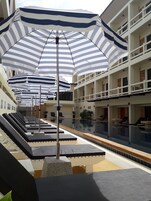 Área de piscina com guarda-sóis listrados, espreguiçadeiras e uma piscina refletora.