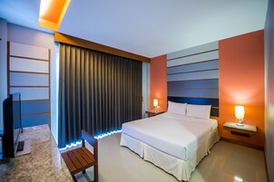 Quarto de hotel moderno com uma cama grande, mesas de cabeceira, escrivaninha e televisão.