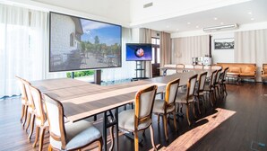 Uma sala de conferências com uma mesa grande, cadeiras, uma tela de TV e um sofá.