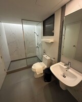 Um banheiro moderno com chuveiro em gabinete de vidro, vaso sanitário e pia.