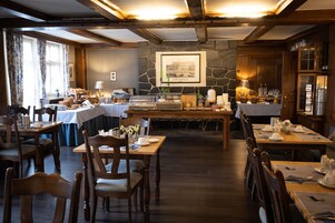 Restaurante com mobiliário de madeira, paredes de pedra e lareira de pedra. Mesas montadas com pratos, copos e talheres.
