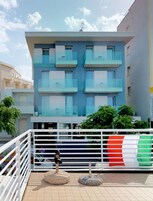 Um edifício moderno de vários andares com varandas, um terraço em mosaico e exibição de bandeiras.