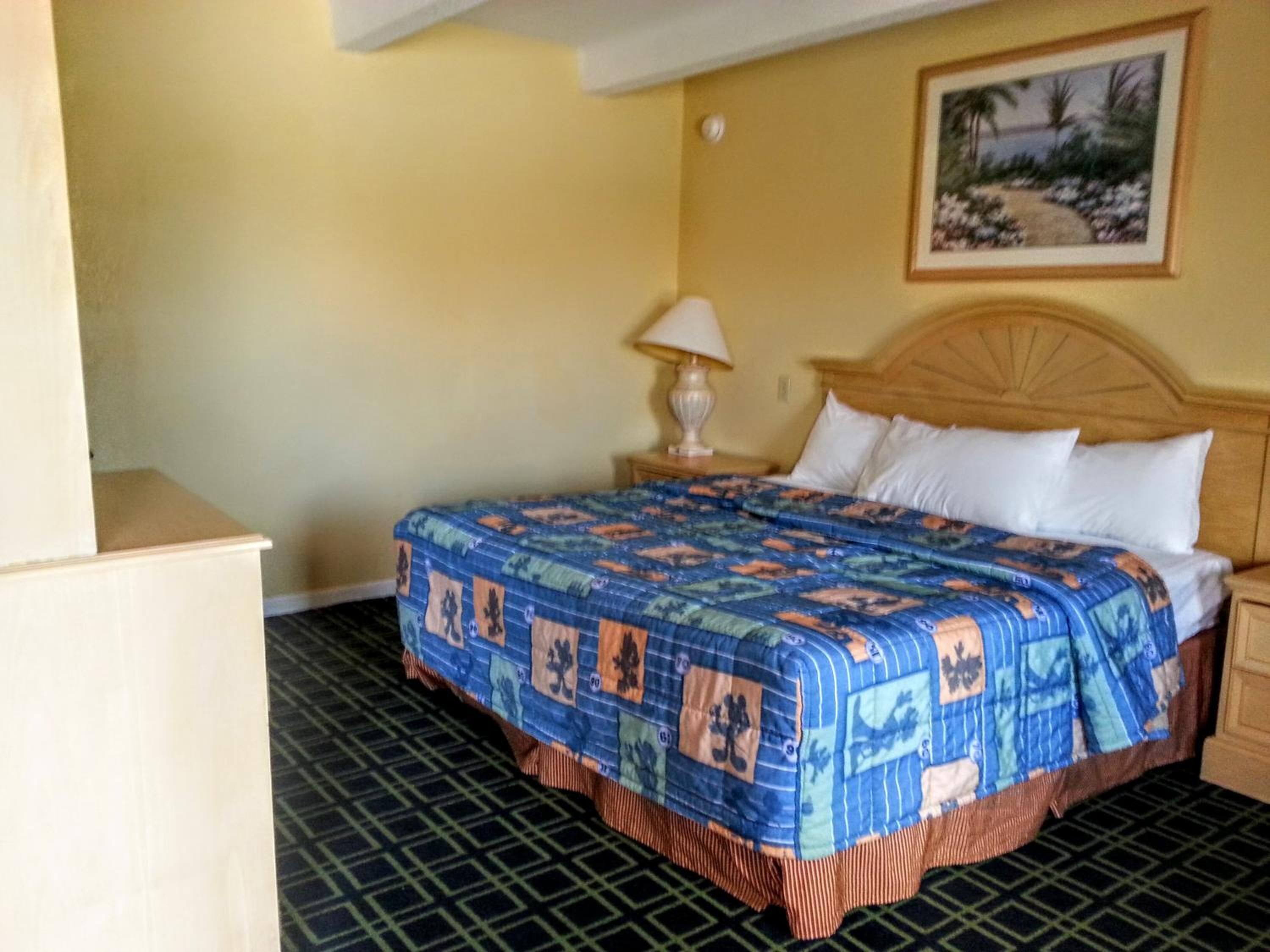 Quarto de hotel com cama, mesa de cabeceira, abajur e um quadro na parede.