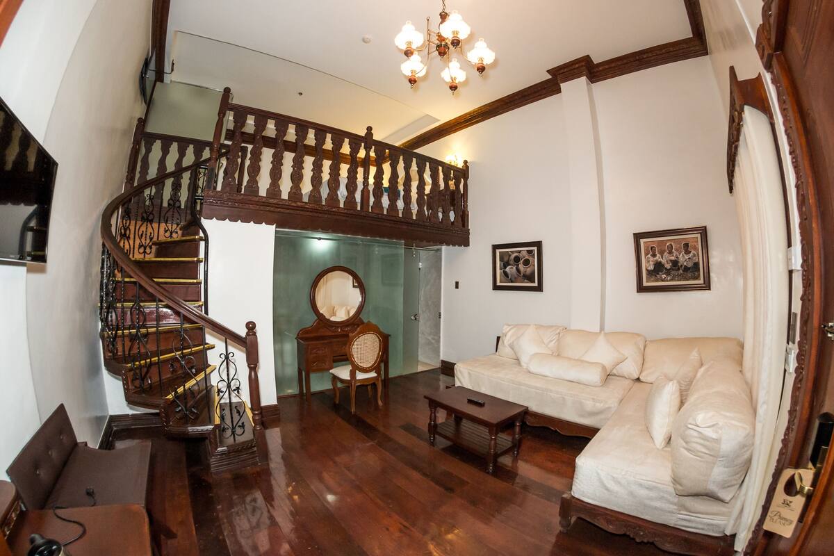 Uma sala de estar espaçosa com escada de madeira, um sofá branco, uma mesa pequena e um espelho.