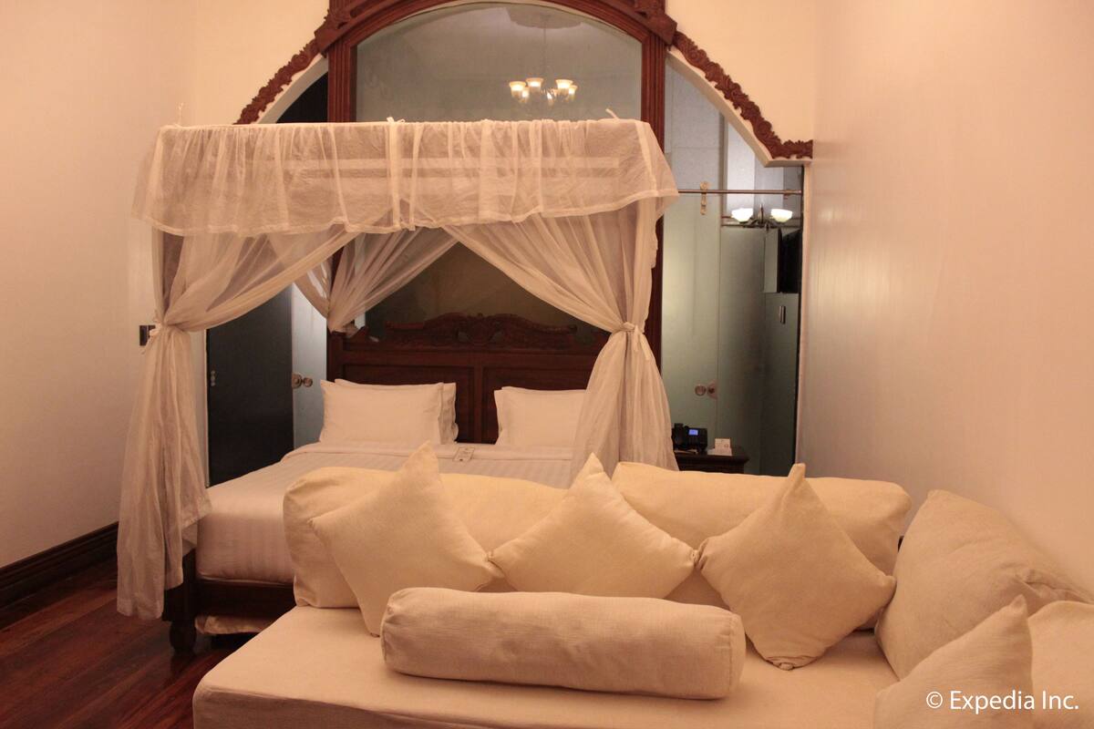 Quarto com cama de dossel, mesa de cabeceira e espelho.