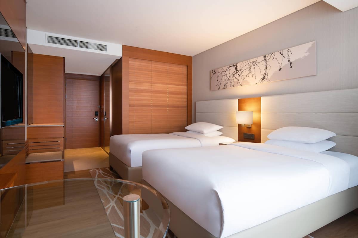 Quarto de hotel com duas camas, uma televisão, guarda-roupa de madeira e uma obra de arte na parede.