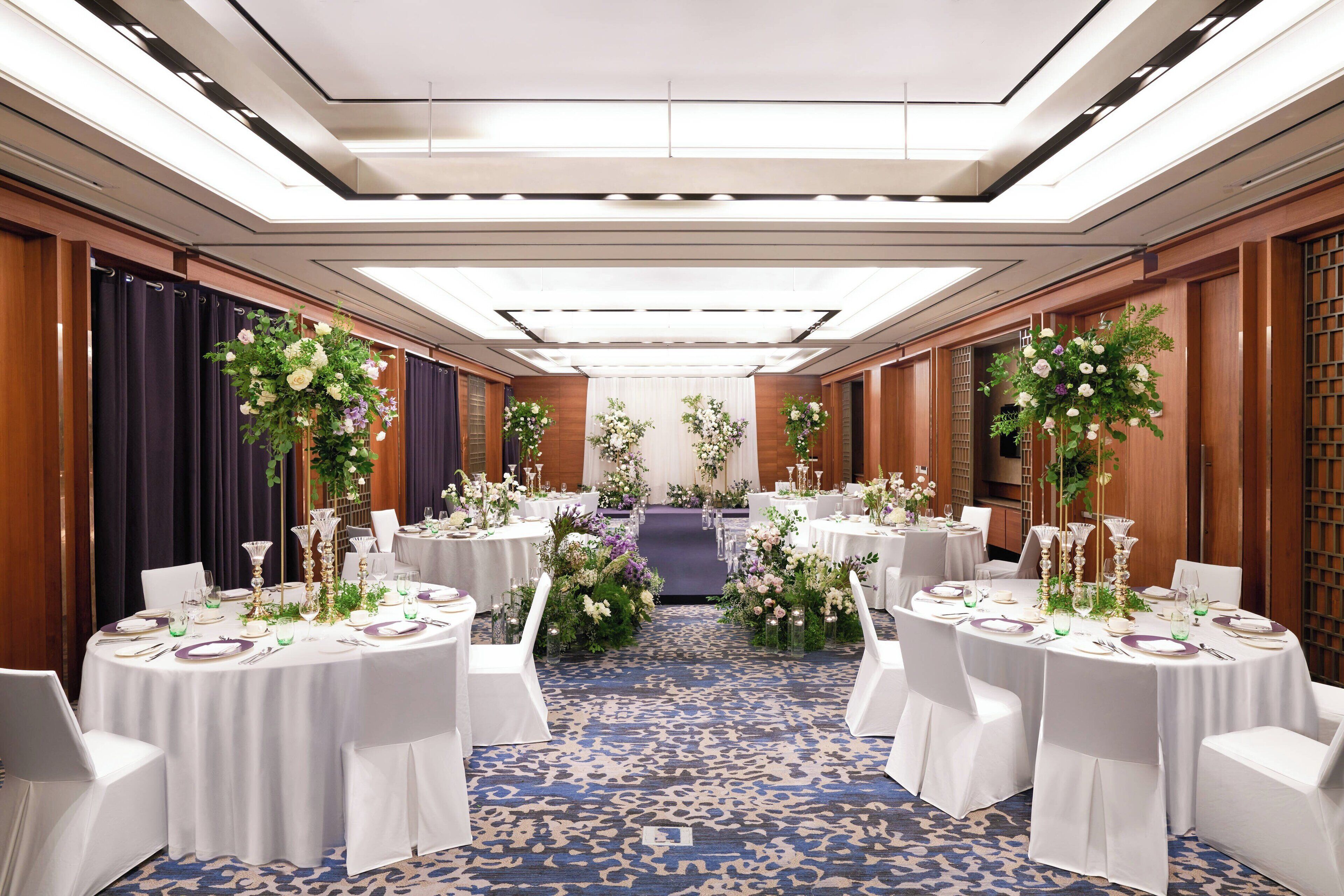 Uma sala de banquetes com mesas redondas, cadeiras brancas e centros de mesa florais.
