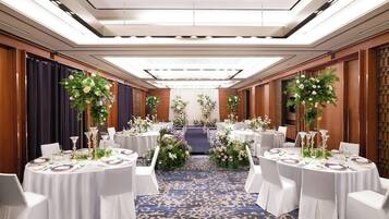 Uma sala de banquetes com mesas redondas, cadeiras brancas e centros de mesa florais.