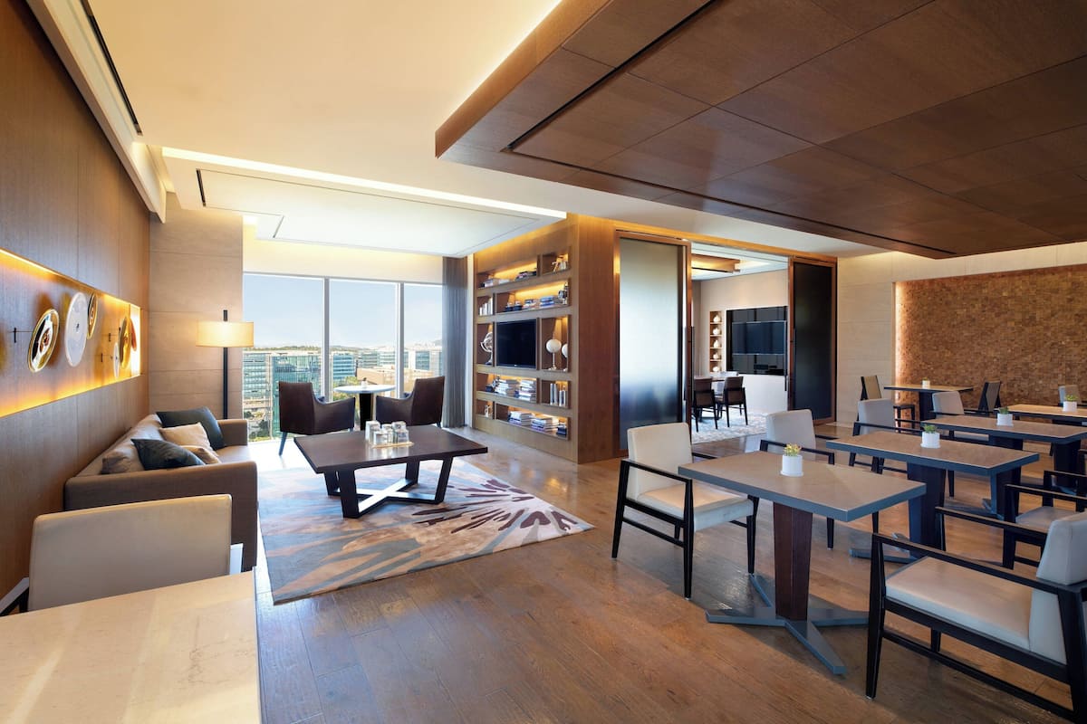 Um hall de hotel moderno com sofá, mesas de jantar, cadeiras, uma estante de livros e vista para a cidade.