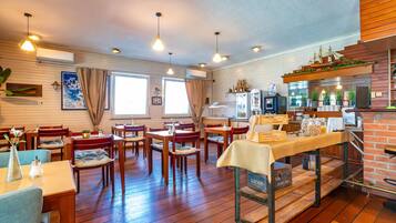 Um restaurante com piso de madeira, cadeiras vermelhas e um espaço de bar com parede de tijolos.