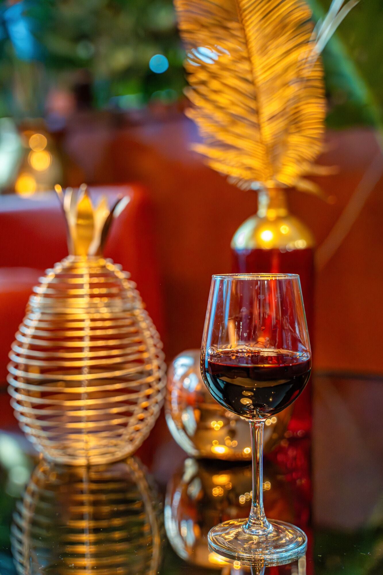 Um copo de vinho tinto sobre uma superfície refletora, com elementos dourados decorativos ao fundo.