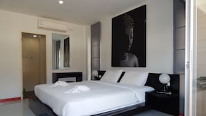 Quarto de hotel moderno com uma cama grande, uma mesinha de cabeceira com abajur, ar-condicionado fixado na parede e um quadro abstrato de grandes dimensões.